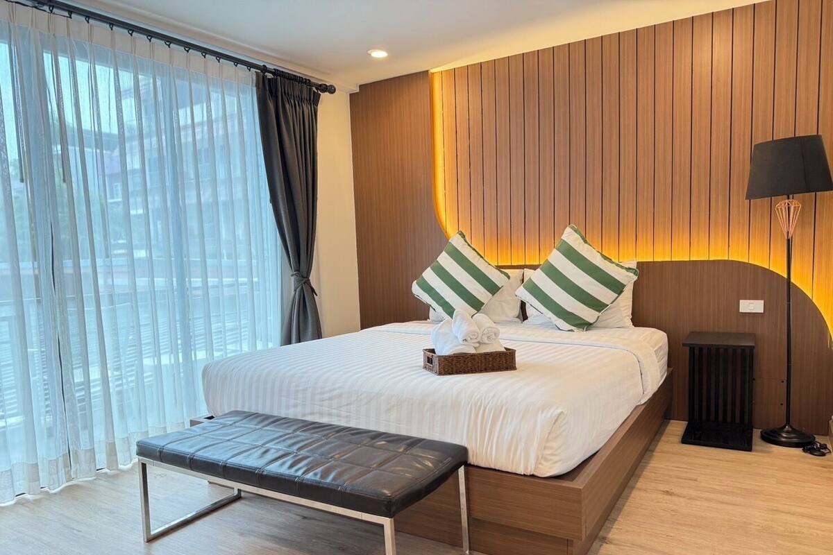 Quarto de hotel moderno com uma cama grande, um banco e um abajur.