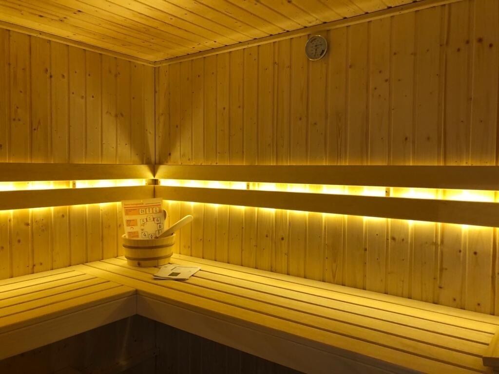 Uma sauna com paredes e bancos de madeira, um relógio na parede e um balde com toalhas.