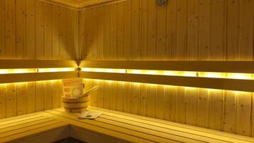 Uma sauna com paredes e bancos de madeira, um relógio na parede e um balde com toalhas.