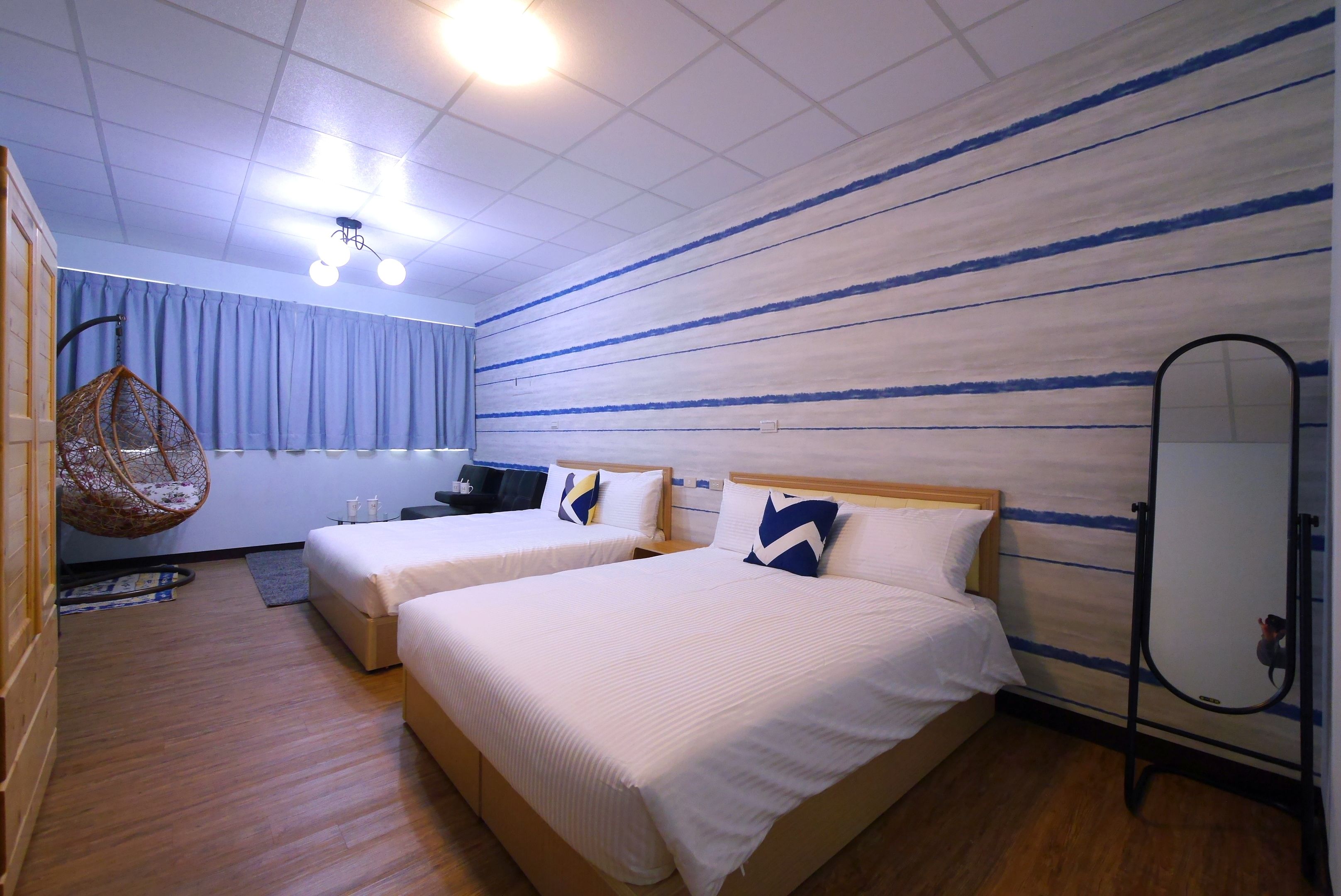 Quarto de hotel com duas camas, uma cadeira suspensa, uma escrivaninha e um espelho.