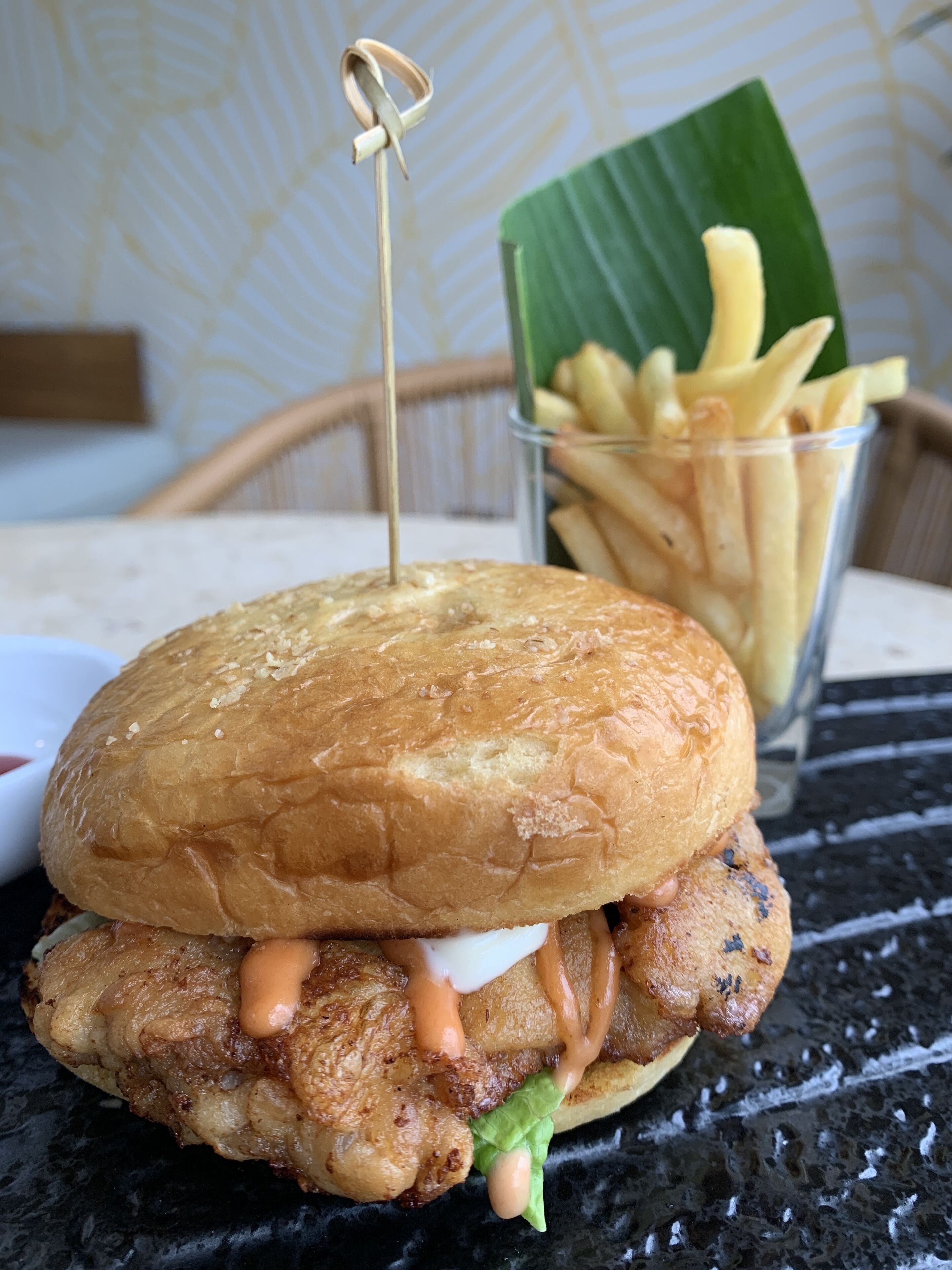 Um sanduíche com um palito, batatas fritas e uma pequena tigela de molho sobre uma mesa.