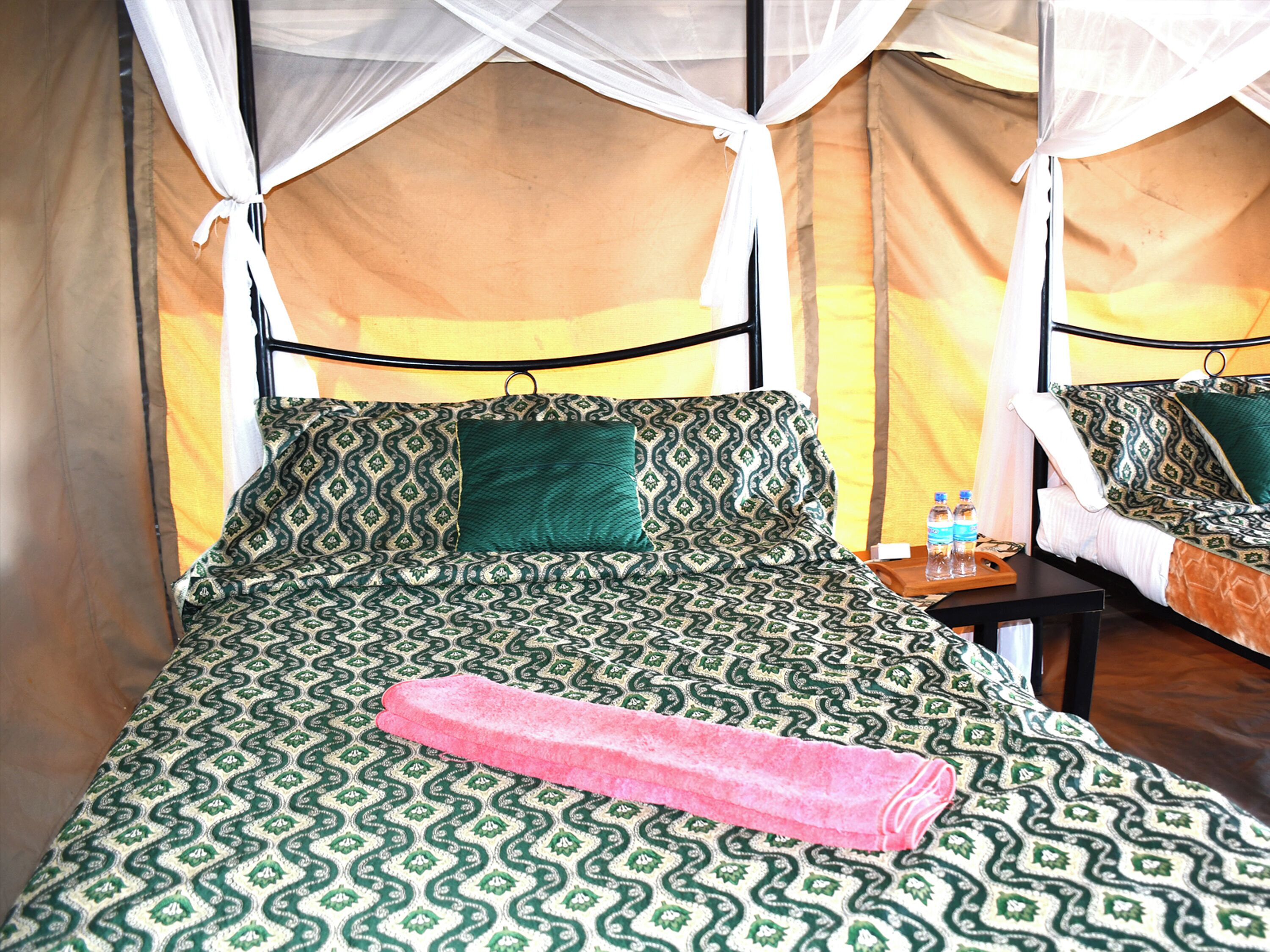 Quarto com cama coberta por roupa de cama estampada, mesa de cabeceira com uma garrafa e mosquiteiro.