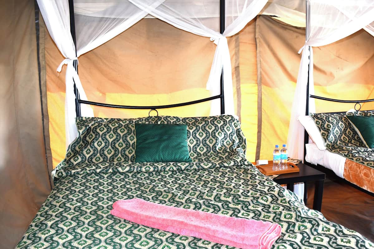 Quarto com cama coberta por roupa de cama estampada, mesa de cabeceira com uma garrafa e mosquiteiro.