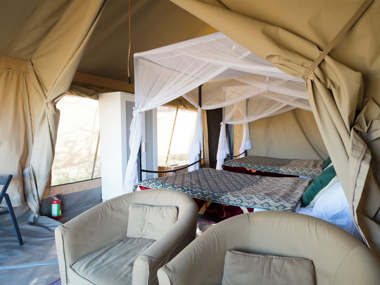 Uma tenda com duas camas, um mosquiteiro e uma cadeira.