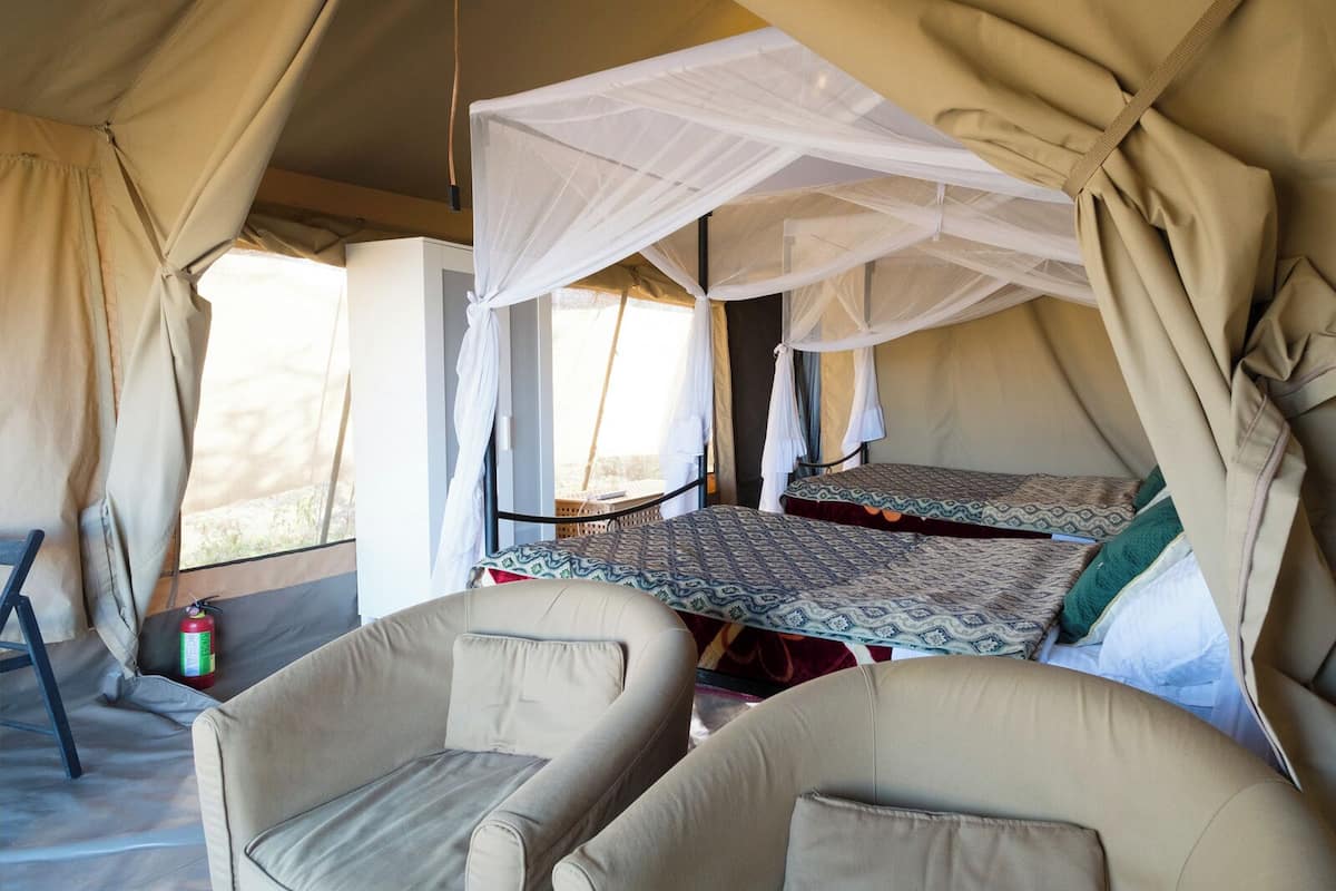 Uma tenda com duas camas, um mosquiteiro e uma cadeira.