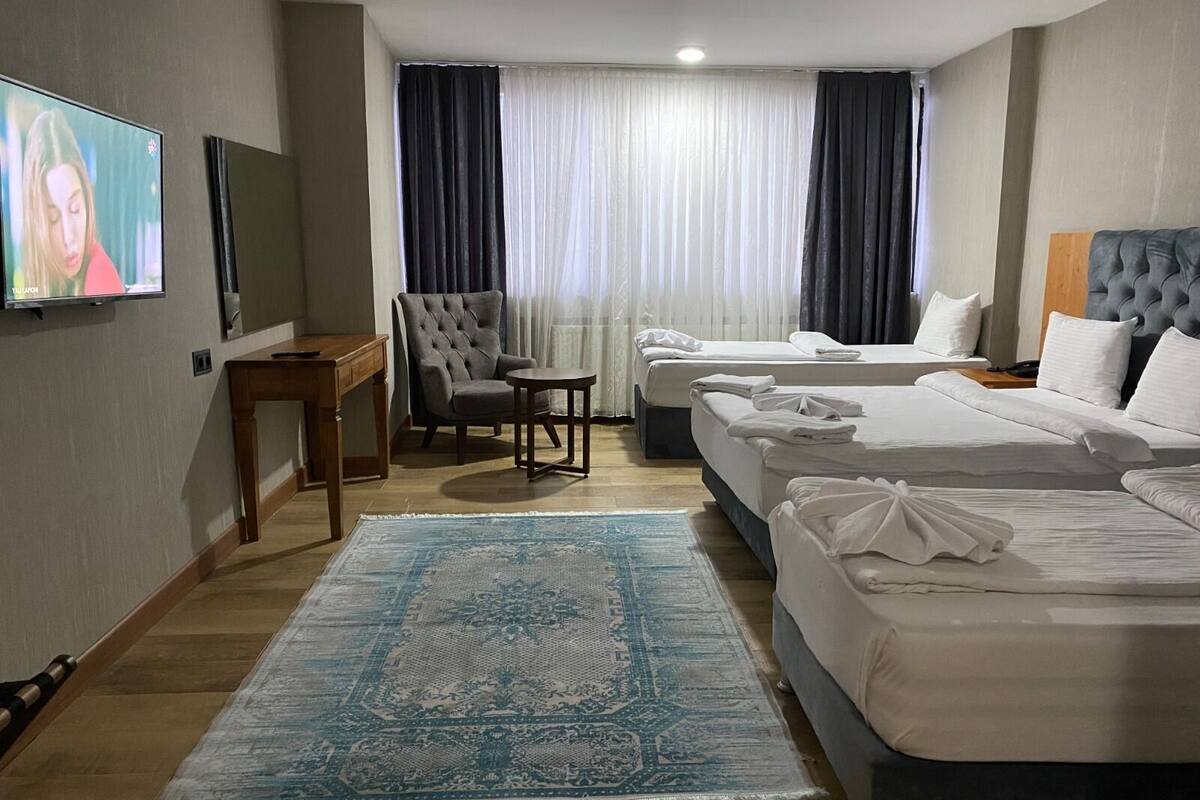 Quarto de hotel com duas camas, televisão, uma cadeira, mesa pequena e tapete azul grande.