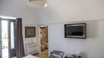 Quarto de hotel com uma cama, televisão na parede, uma mesa pequena com um controle remoto e uma porta que dá para um banheiro.