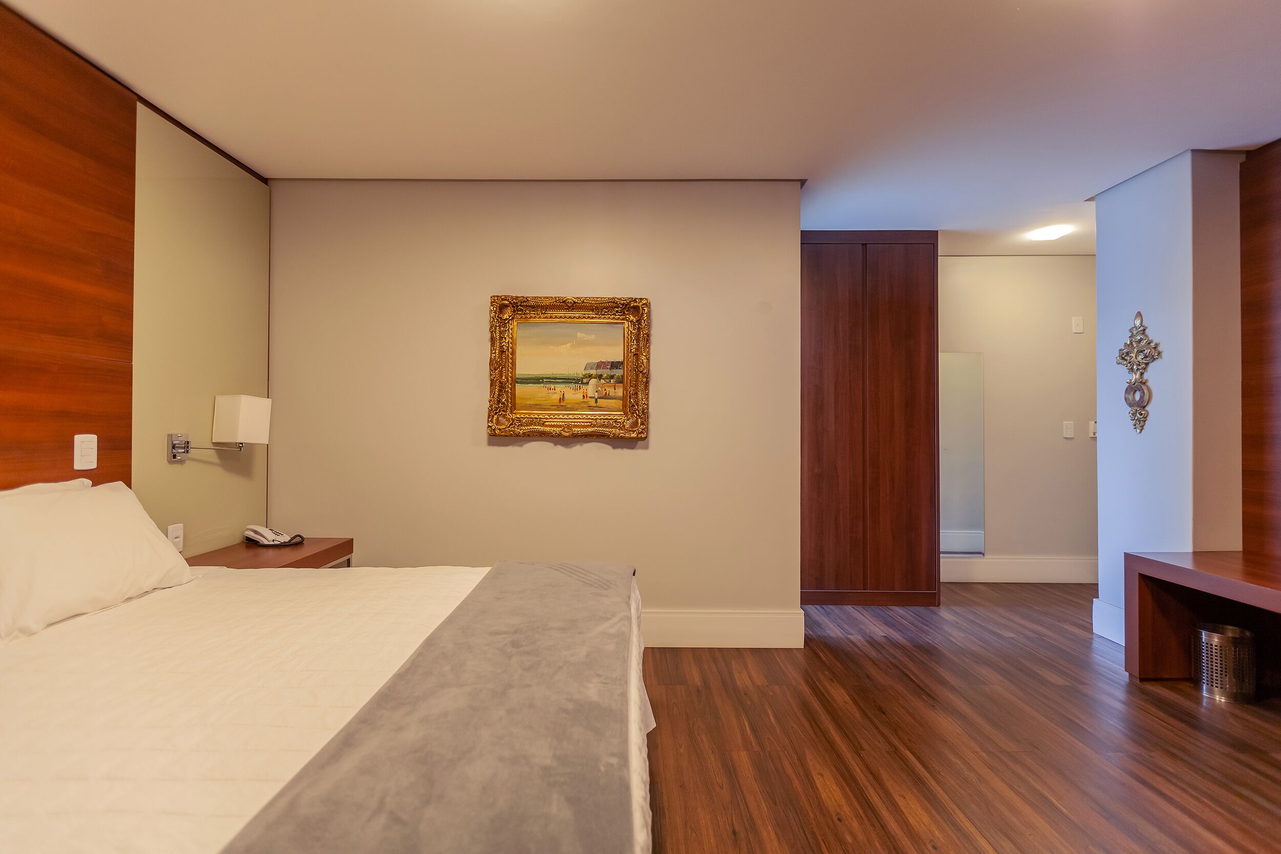 Quarto de hotel com cama, mesa de cabeceira, abajur e um quadro na parede.