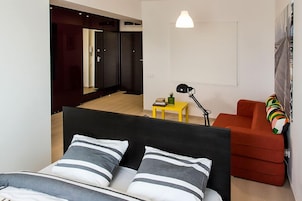 Quarto moderno com cama, uma cadeira vermelha, uma mesinha com abajur e um espelho.