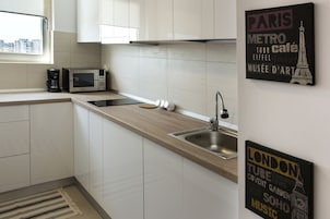 Uma cozinha moderna com armários brancos, uma pia de aço inoxidável e um micro-ondas. Há dois letreiros na parede, um com texto relacionado a Paris e outro com texto relacionado a Londres.