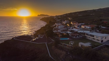 Uma vila costeira com casas, piscina e vista desobstruída do pôr do sol sobre o mar.