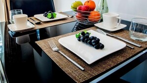 Uma mesa de jantar posta com pratos de uvas e maçãs, um vaso com uma única flor e um copo de água.