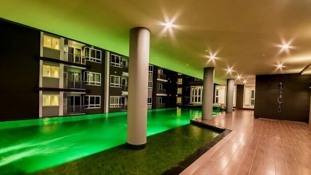 Piscina interior moderna com um recurso aquático iluminado em verde, rodeada por um espaço amplo com soalho de madeira e teto alto.