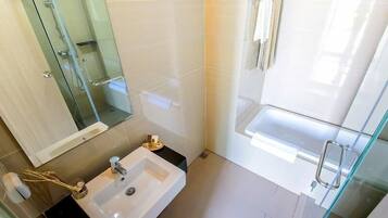 Uma casa de banho moderna com cabine de duche em vidro, lavatório branco e espelho grande.