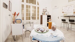 Uma área de refeições com uma mesa redonda, cadeiras e uma mesa com tampo de vidro. Há uma janela com vista para o exterior.