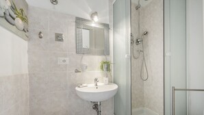 Casa de banho moderna com lavatório branco, cabine de duche em vidro e espelho decorativo.