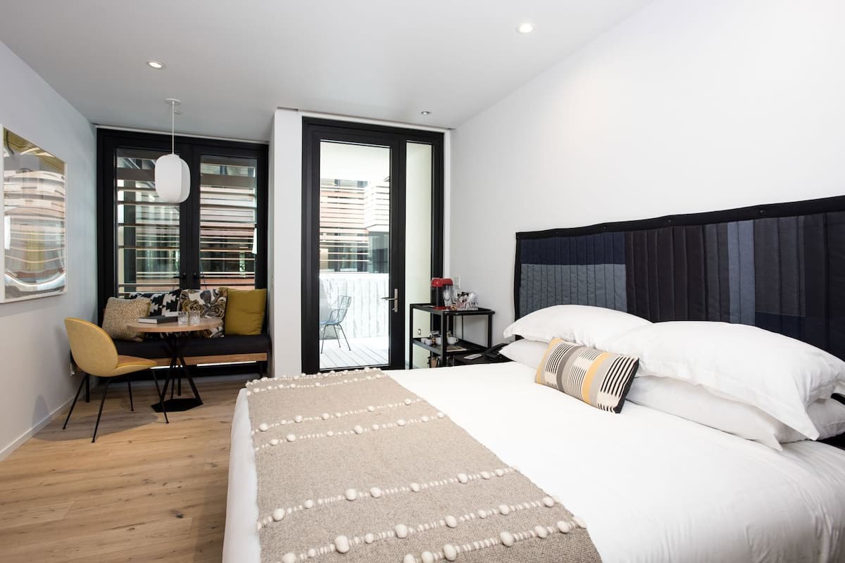 Quarto de hotel moderno com uma cama grande, uma escrivaninha com cadeira, um sofá e uma varanda com vista.
