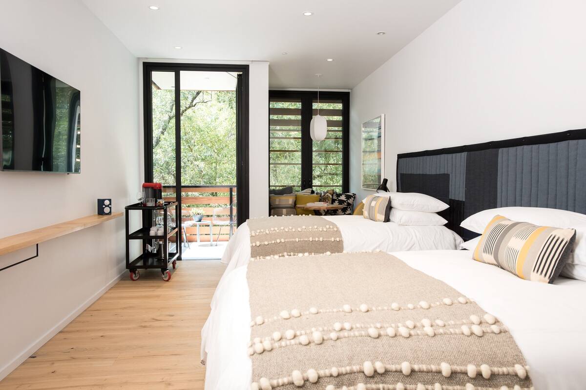 Quarto moderno com duas camas, uma janela grande e varanda.