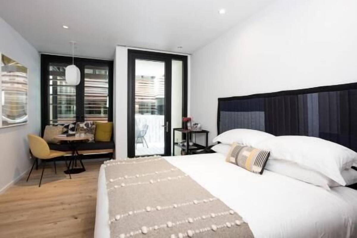 Quarto de hotel moderno com uma cama grande, uma escrivaninha e vista através de uma porta de vidro.