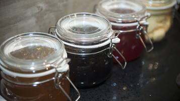 Vários potes de vidro com tampas e alças de metal, provavelmente contendo alimentos, dispostos sobre uma superfície refletora.