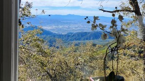 Janela com vista para uma paisagem montanhosa, um vaso de planta e uma mesa.