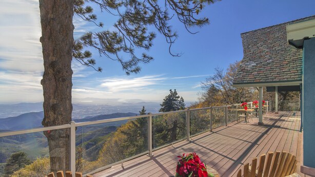 Um deck de madeira com cadeiras e uma mesa, com vista para uma paisagem deslumbrante com montanhas e árvores.