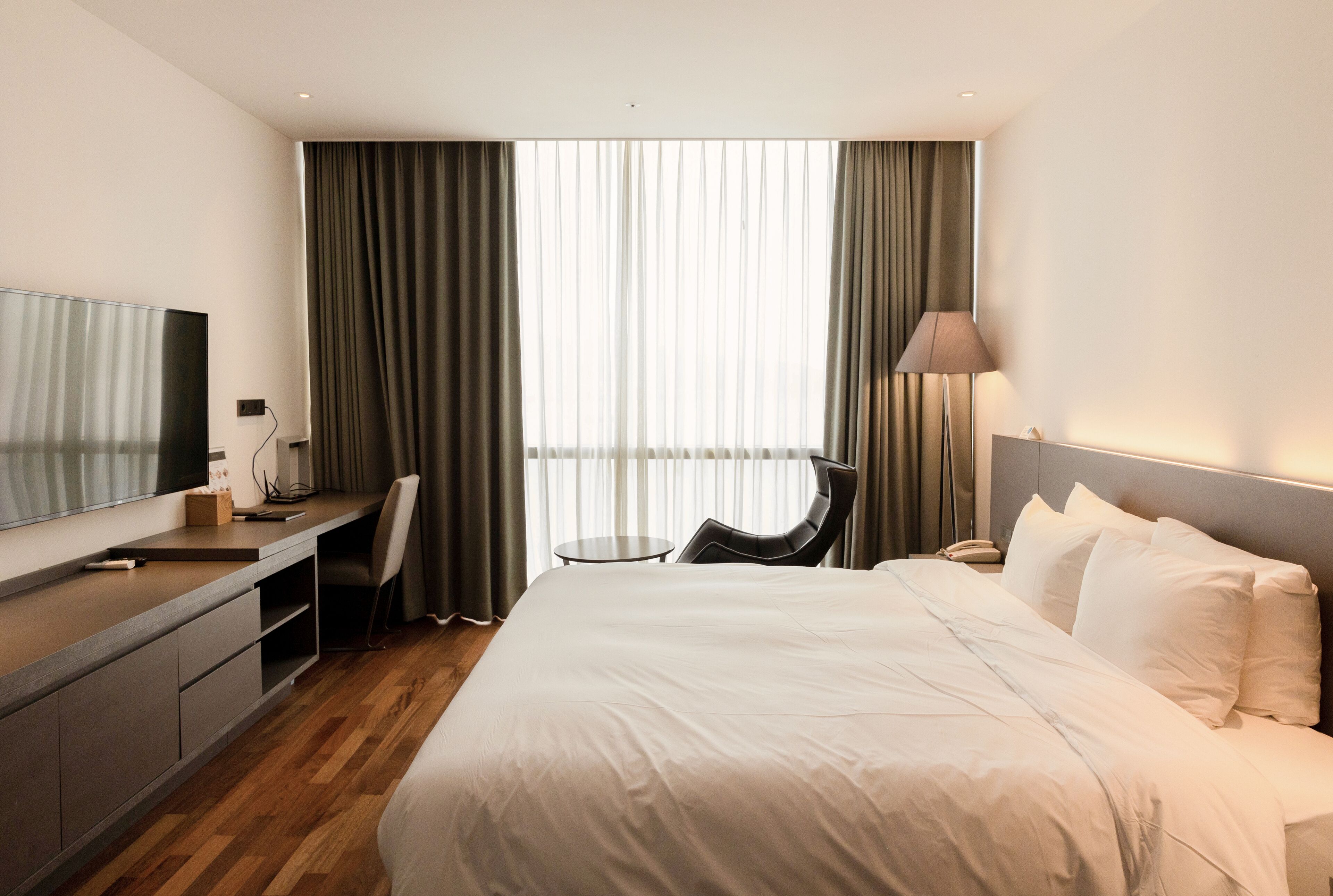 Quarto de hotel com cama grande, escrivaninha com cadeira, televisão e luminária.