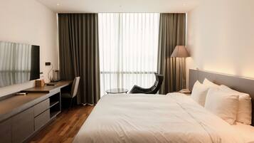 Quarto de hotel com cama grande, escrivaninha com cadeira, televisão e luminária.