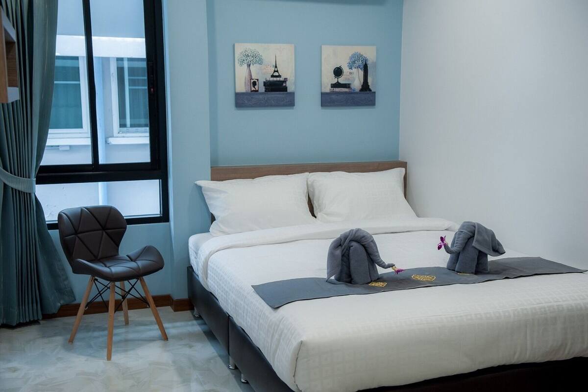 Quarto de hotel com cama, uma cadeira, duas pinturas na parede e janela com cortinas.