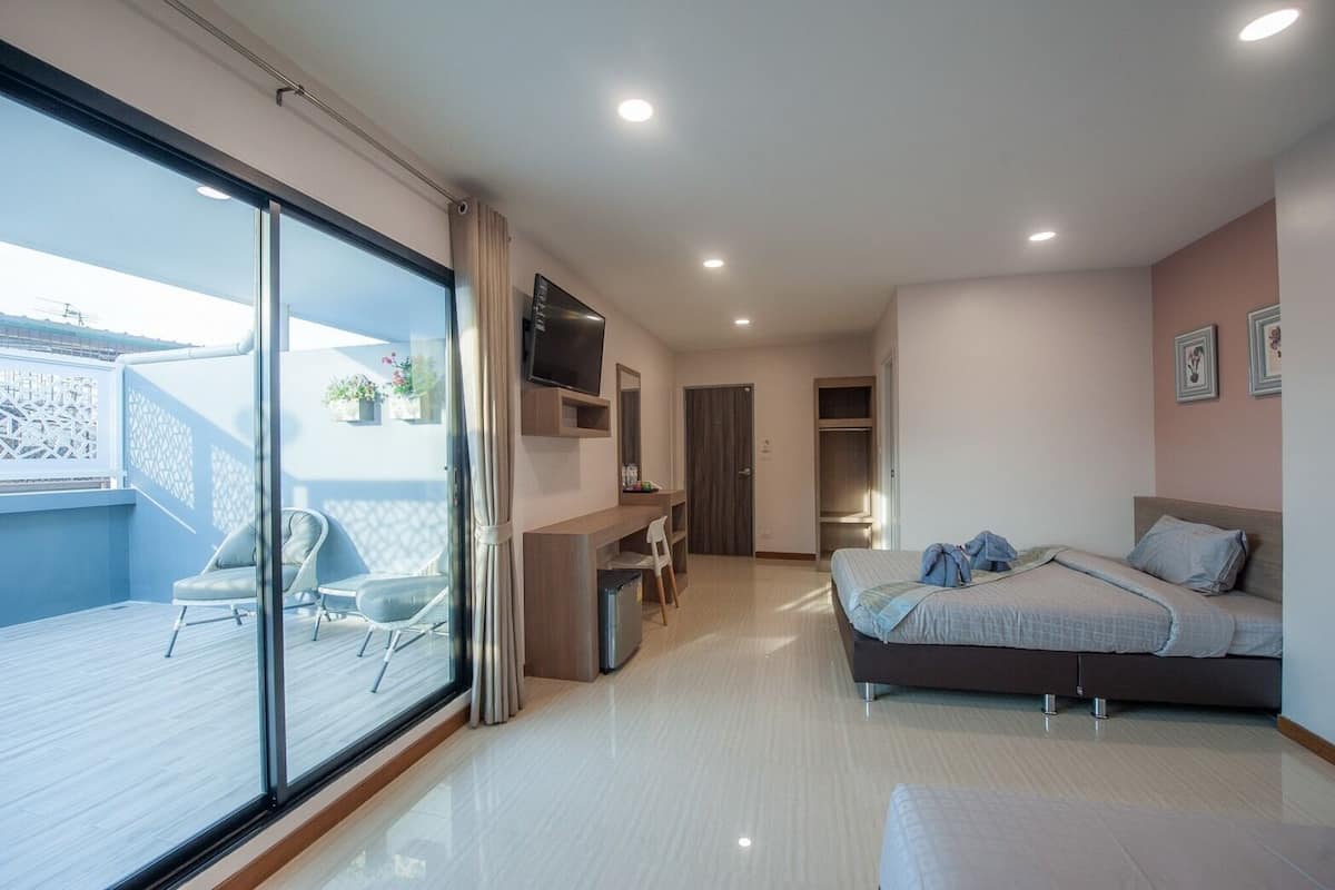 Quarto moderno com cama, escrivaninha, televisão e varanda com uma cadeira.