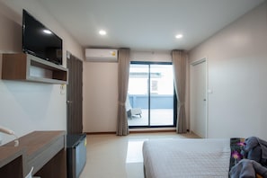 Quarto de hotel com cama, televisão fixada na parede, escrivaninha com cadeira e porta de vidro deslizante para uma varanda.