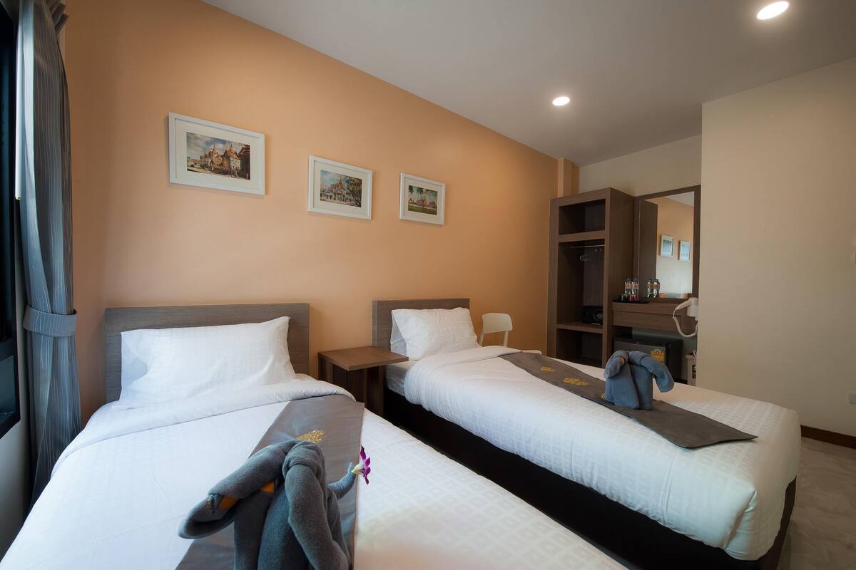 Quarto de hotel com duas camas, um guarda-roupa, um espelho e duas imagens emolduradas na parede.