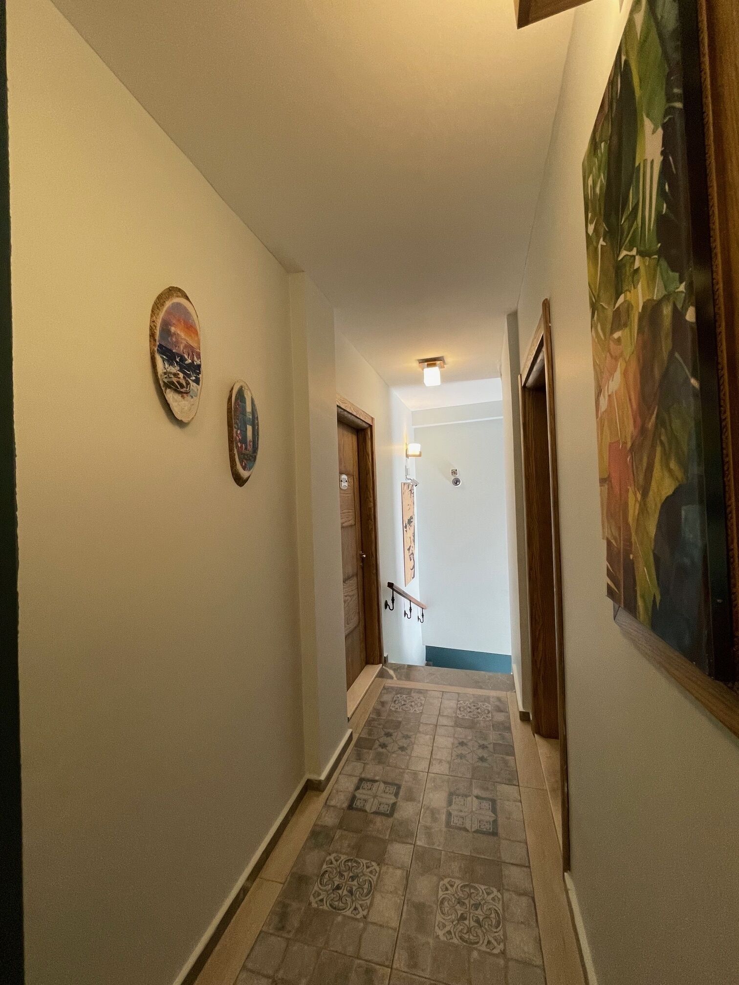 Um corredor com ladrilhos estampados, uma porta de madeira e duas obras de arte emolduradas nas paredes.