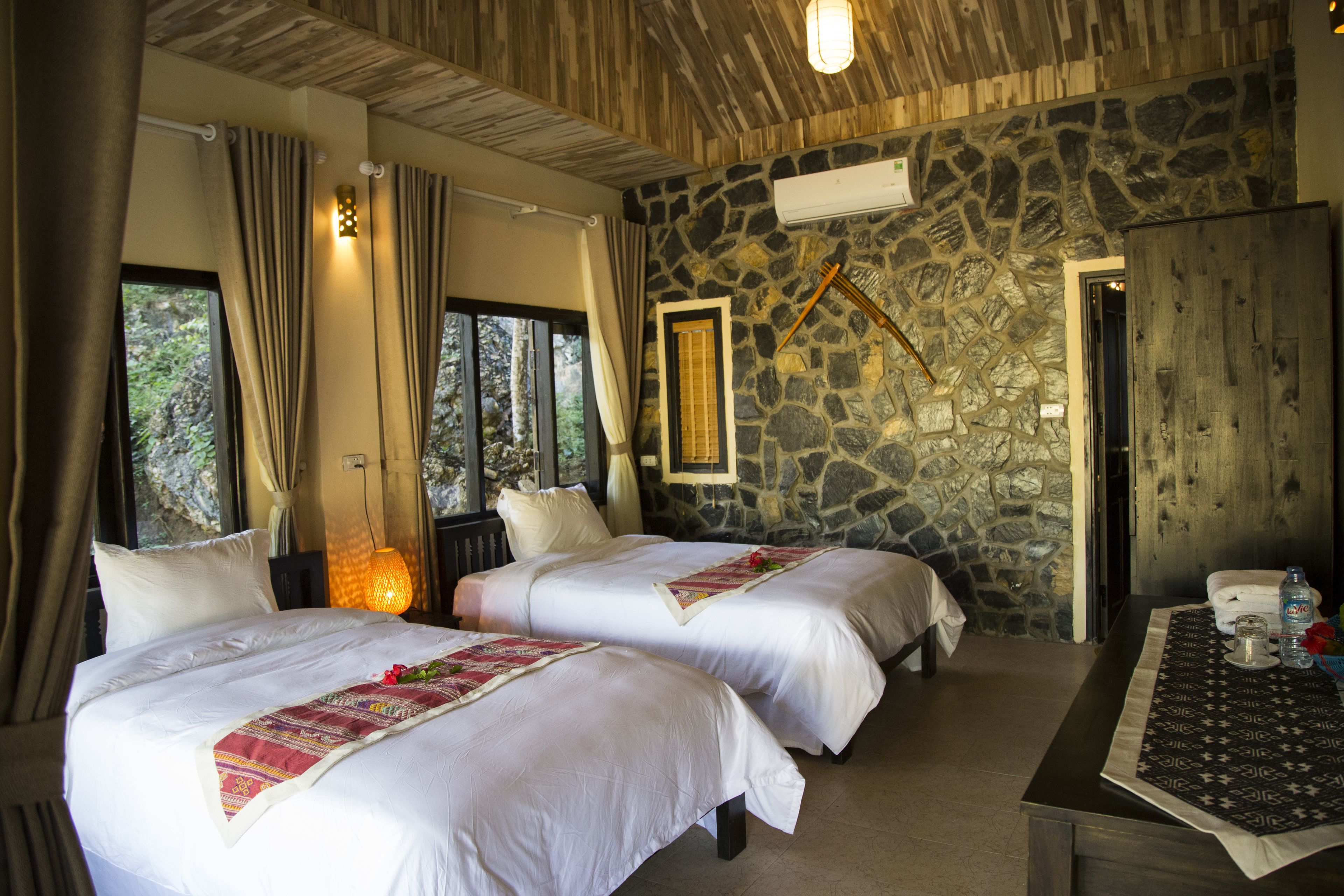 Quarto com duas camas, parede de pedra, teto de madeira e uma mesa com comodidades.