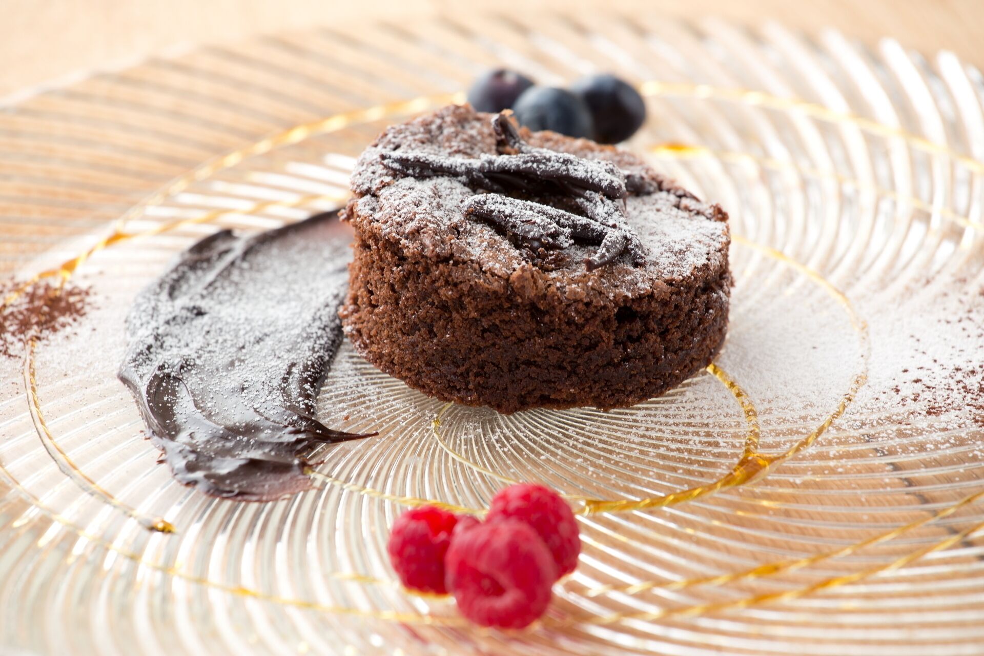Bolo de chocolate com guarnição de framboesas em um prato de vidro.