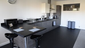 Cozinha moderna com ilha central, banquetas, relógio e eletrodomésticos de aço inoxidável.