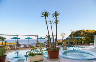 Área de piscina com espreguiçadeiras e guarda-sóis, uma banheira de hidromassagem e vista para o mar.