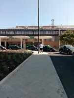 Uma área de estacionamento com carros, uma passarela para pedestres e um edifício com telhado verde e uma ponte para pedestres em cima.