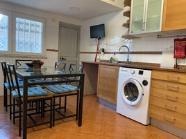 Uma cozinha compacta com máquina de lavar, mesa de jantar com cadeiras, TV fixada acima da pia e janela com vista.