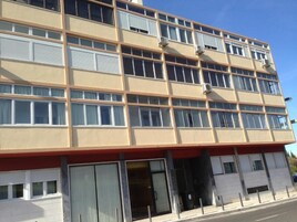 Um edifício de vários andares com fachada bege, grandes janelas e aparelhos de ar condicionado.