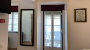 Quarto de hotel com um espelho grande, uma janela com cortina estampada e um quadro na parede.