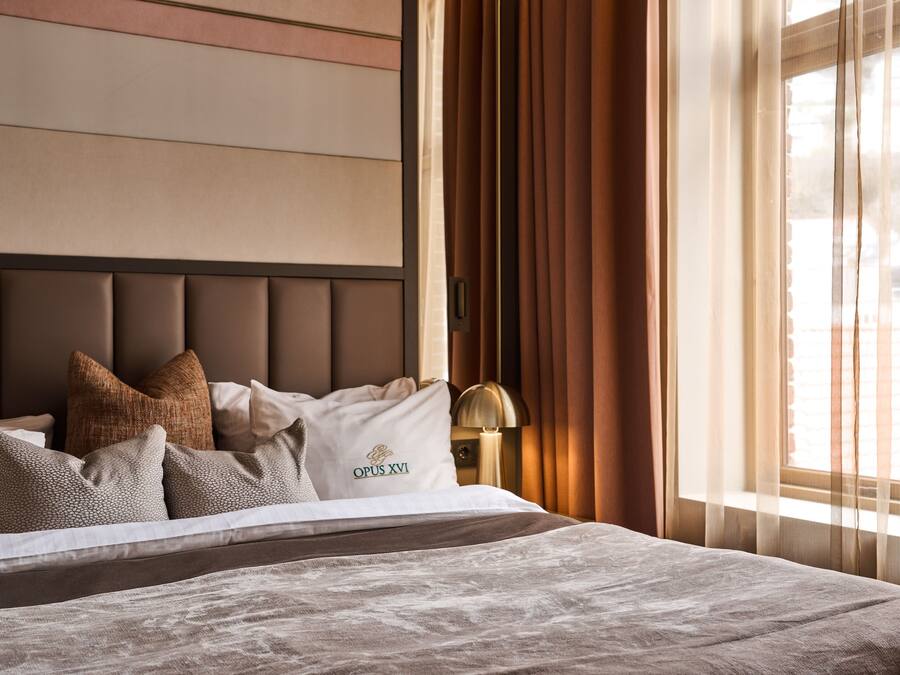 Quarto de hotel com uma cama grande, cabeceira e janela com cortinas.