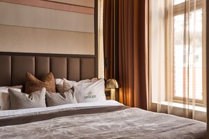 Quarto de hotel com uma cama grande, cabeceira e janela com cortinas.