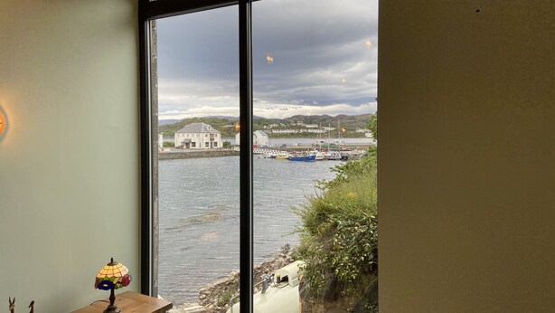 Quarto com uma grande janela com vista para um porto, uma luminária em uma mesa lateral e teto rústico.
