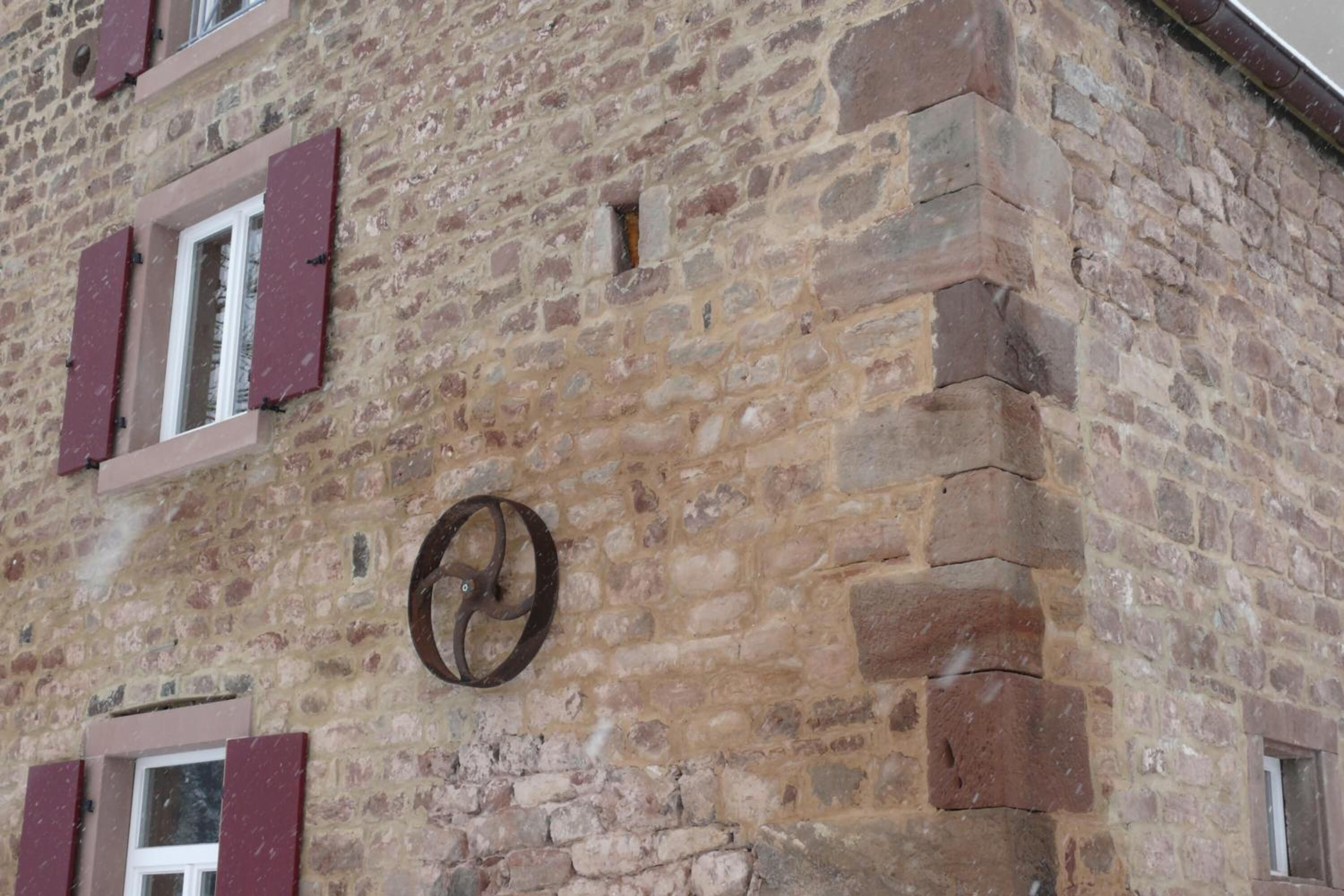 Um edifício de pedra com venezianas vermelhas e um objeto circular grande na parede.