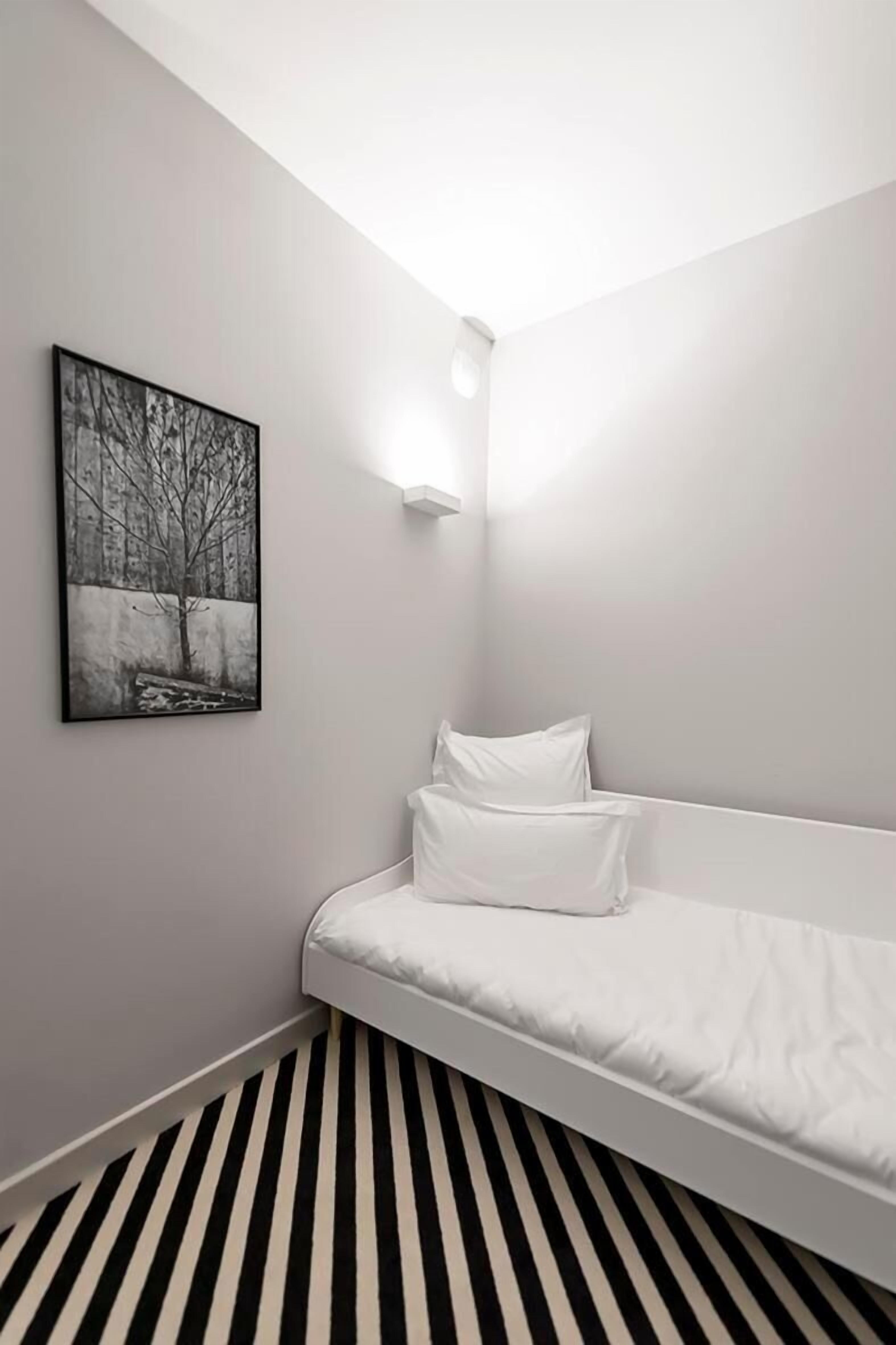 Quarto pequeno e moderno com uma cama de solteiro, piso listrado em preto e branco, e um quadro na parede.