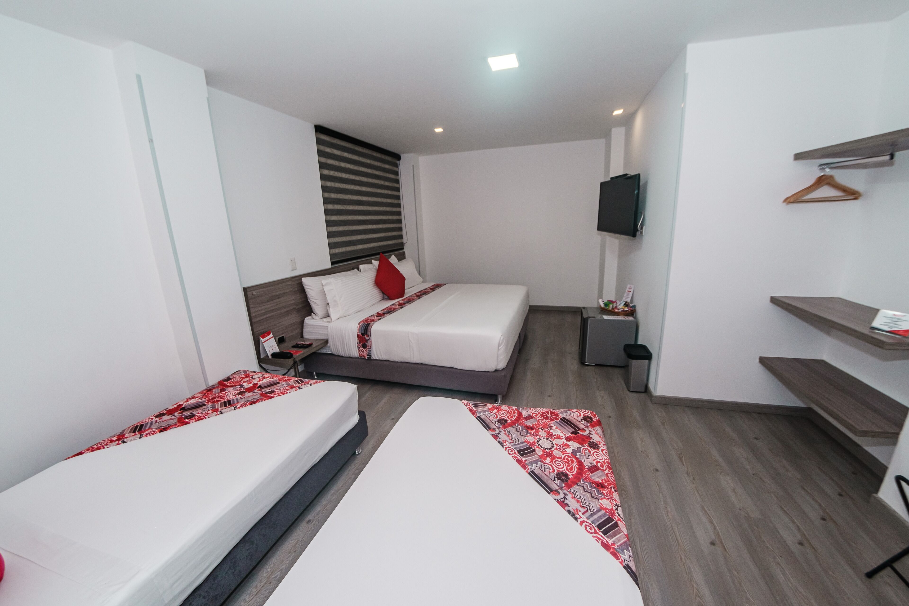 Quarto de hotel moderno com duas camas de solteiro, televisão fixada na parede, pequena escrivaninha e piso de madeira.
