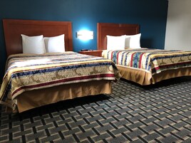 Duas camas de casal com roupa de cama listrada, uma mesa de cabeceira, uma luminária na parede e um tapete estampado.