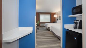 Quarto de hotel com cama, escrivaninha com micro-ondas, máquina de café e pequena geladeira.
