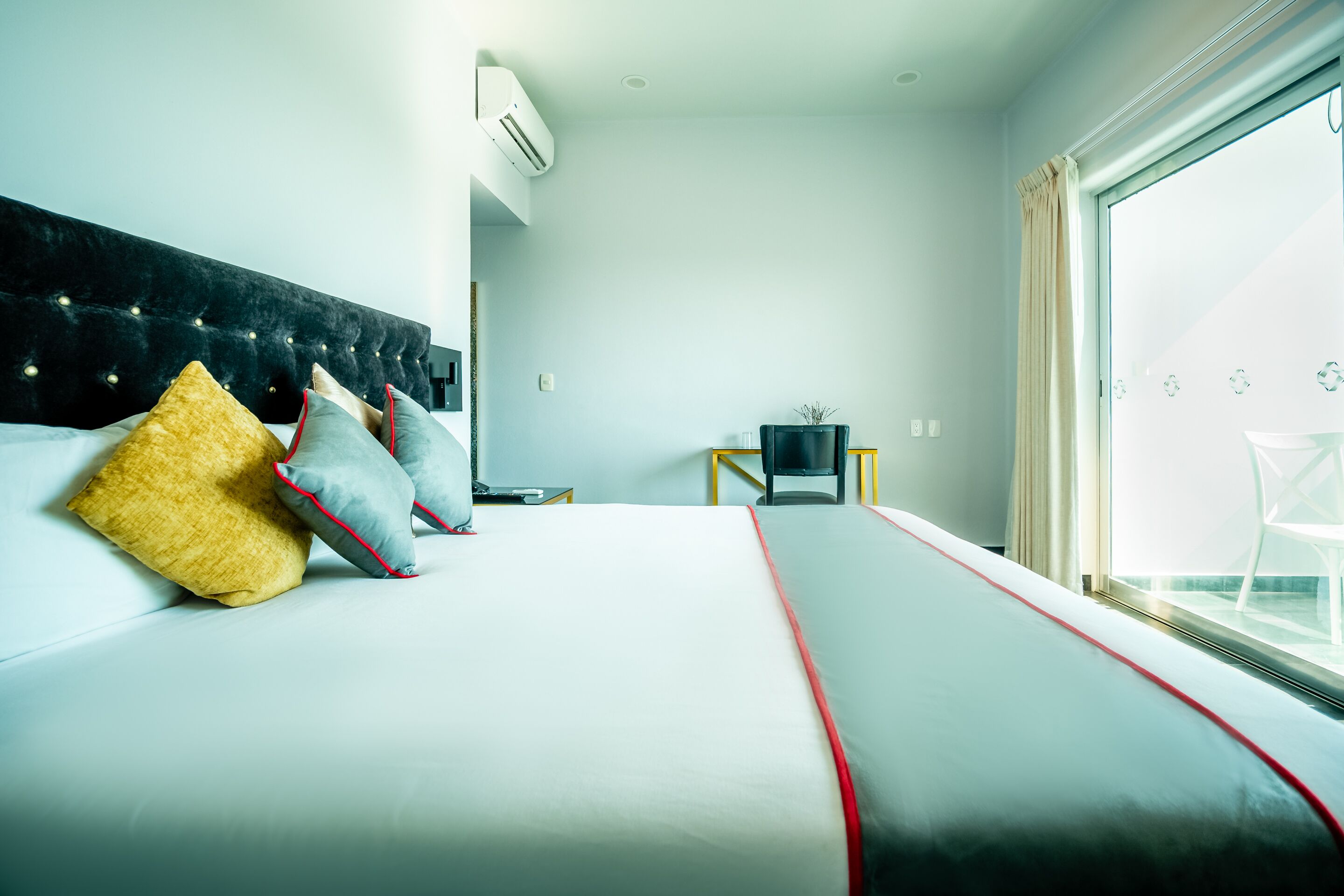 Quarto de hotel moderno com uma cama grande, televisão de tela plana, uma mesinha e uma janela com cortinas.